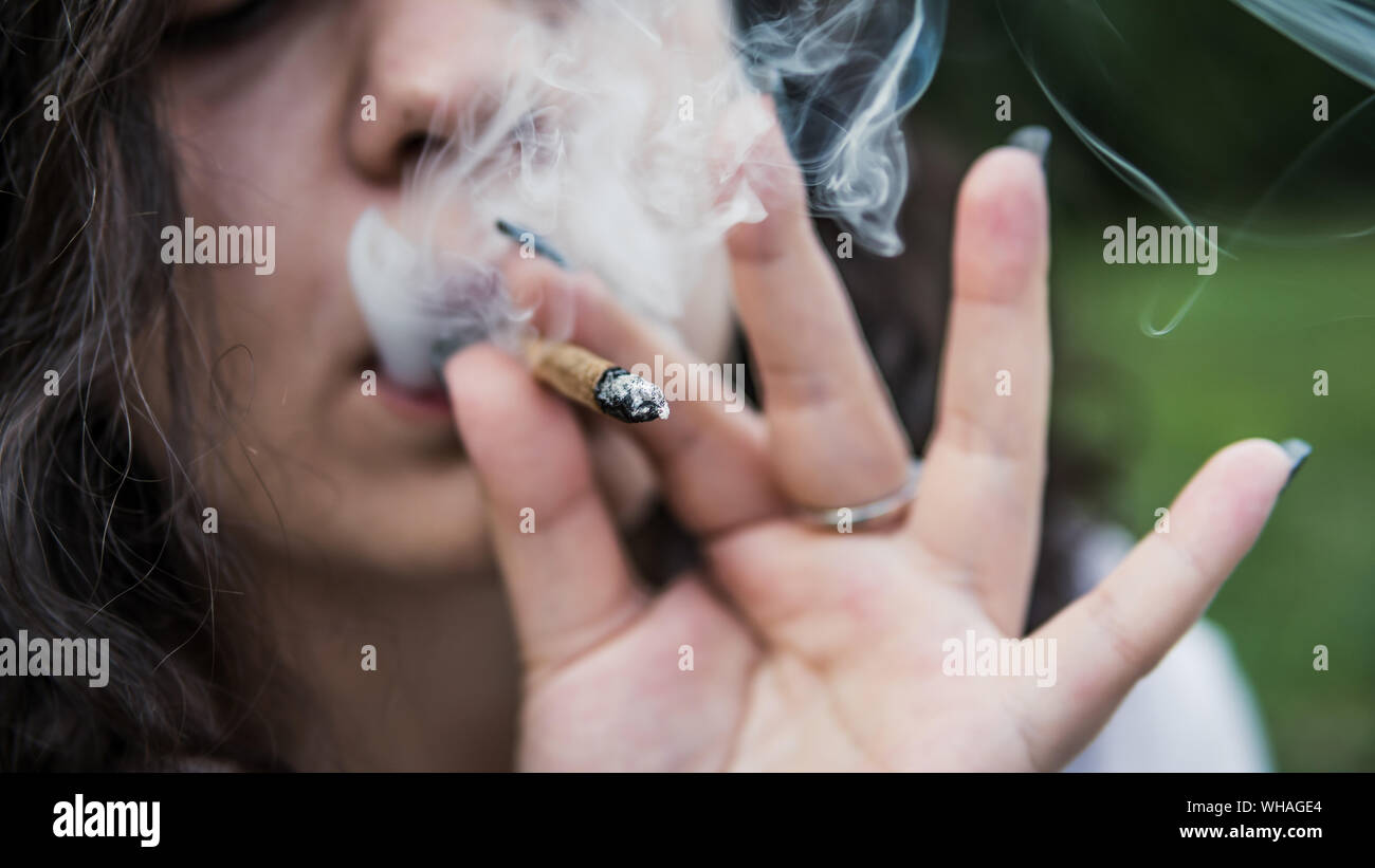 Girl smoking medical marijuana joint outdoors. The young women smoke cannabis blunt, close-up ...