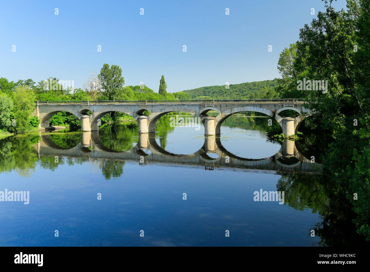 Multi-arched stone bridge over quiet river in France with man fishing ...