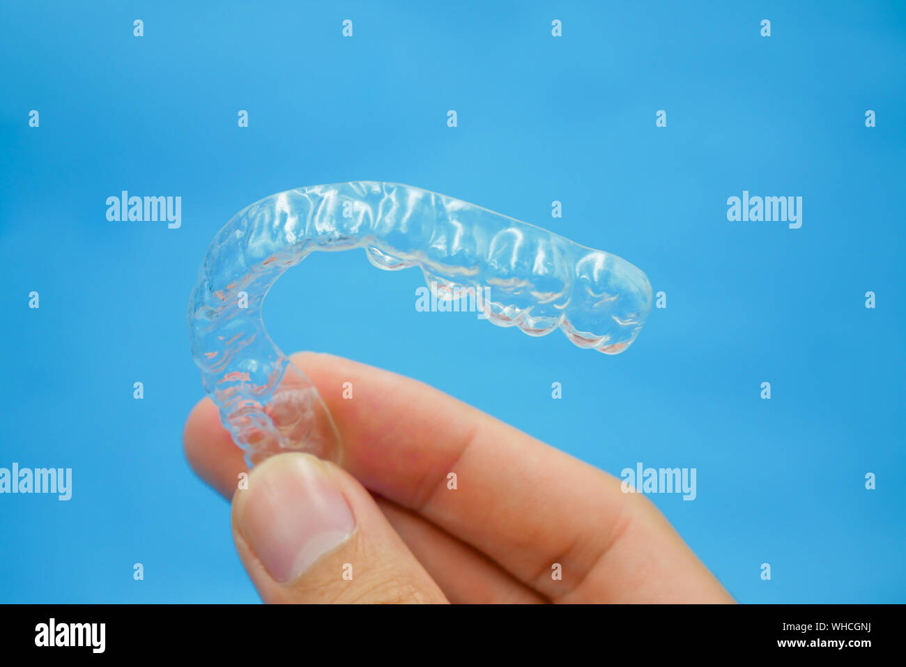 hand holding clear plastic retainer teeth that isolated on blue sky ...