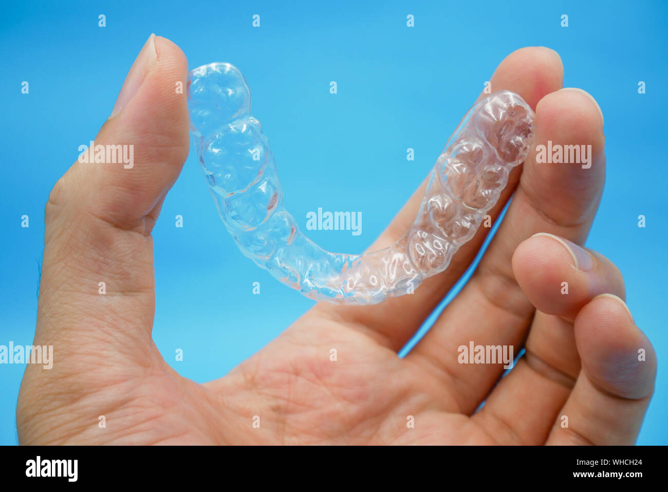 hand holding clear plastic retainer teeth that isolated on blue sky ...