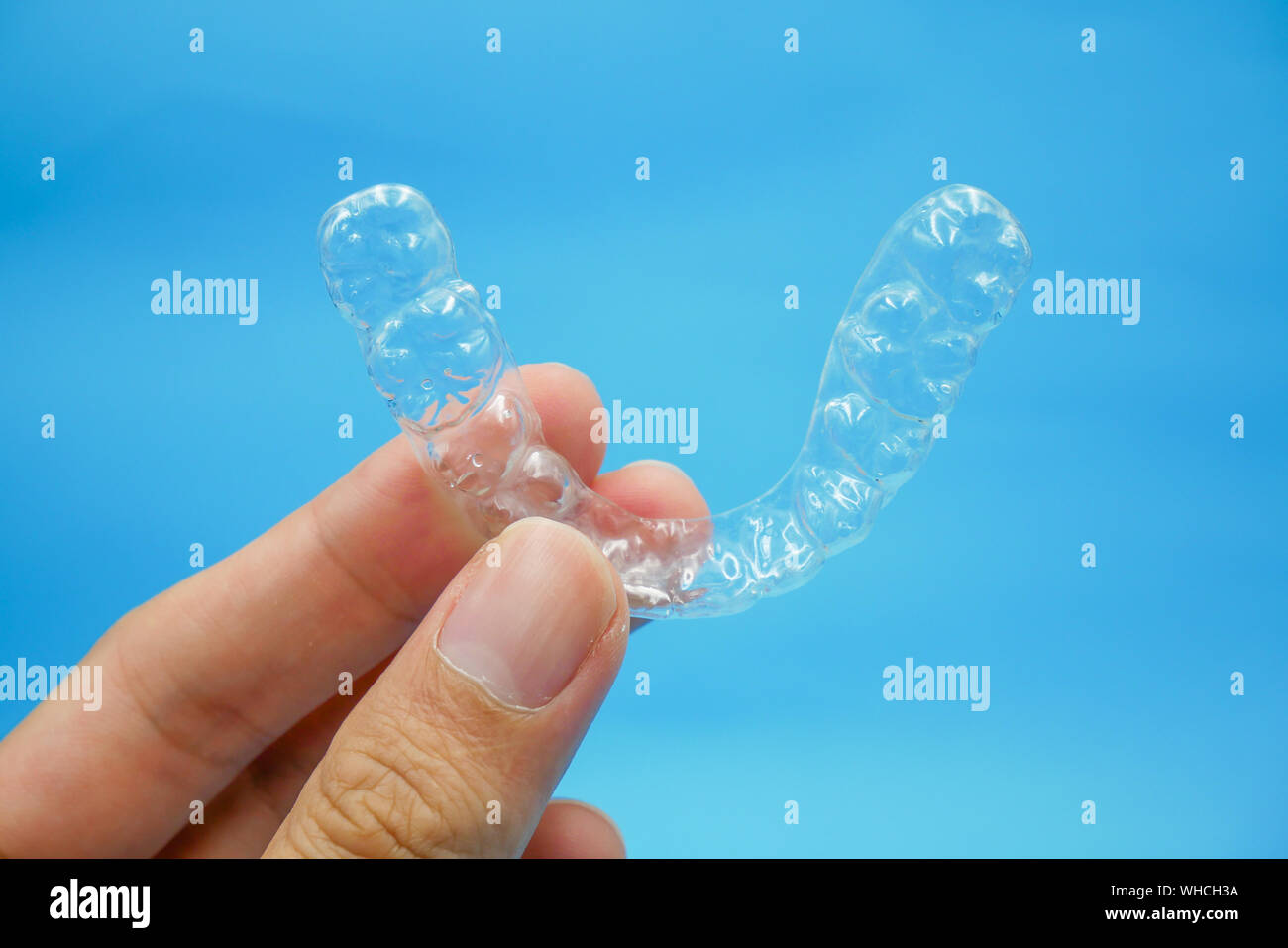 hand holding clear plastic retainer teeth that isolated on blue sky ...