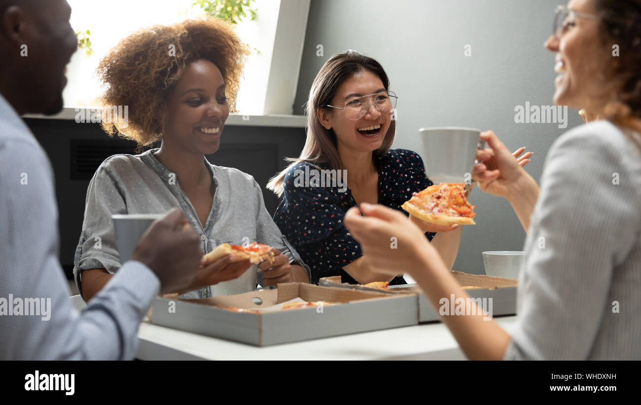 Joyful friendly multicultural team having fun eating pizza together ...