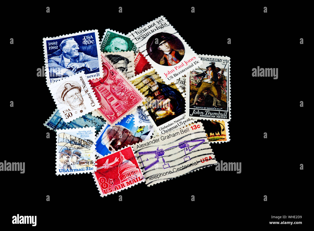 A pile of assorted USA postage stamps isolated against a black ...