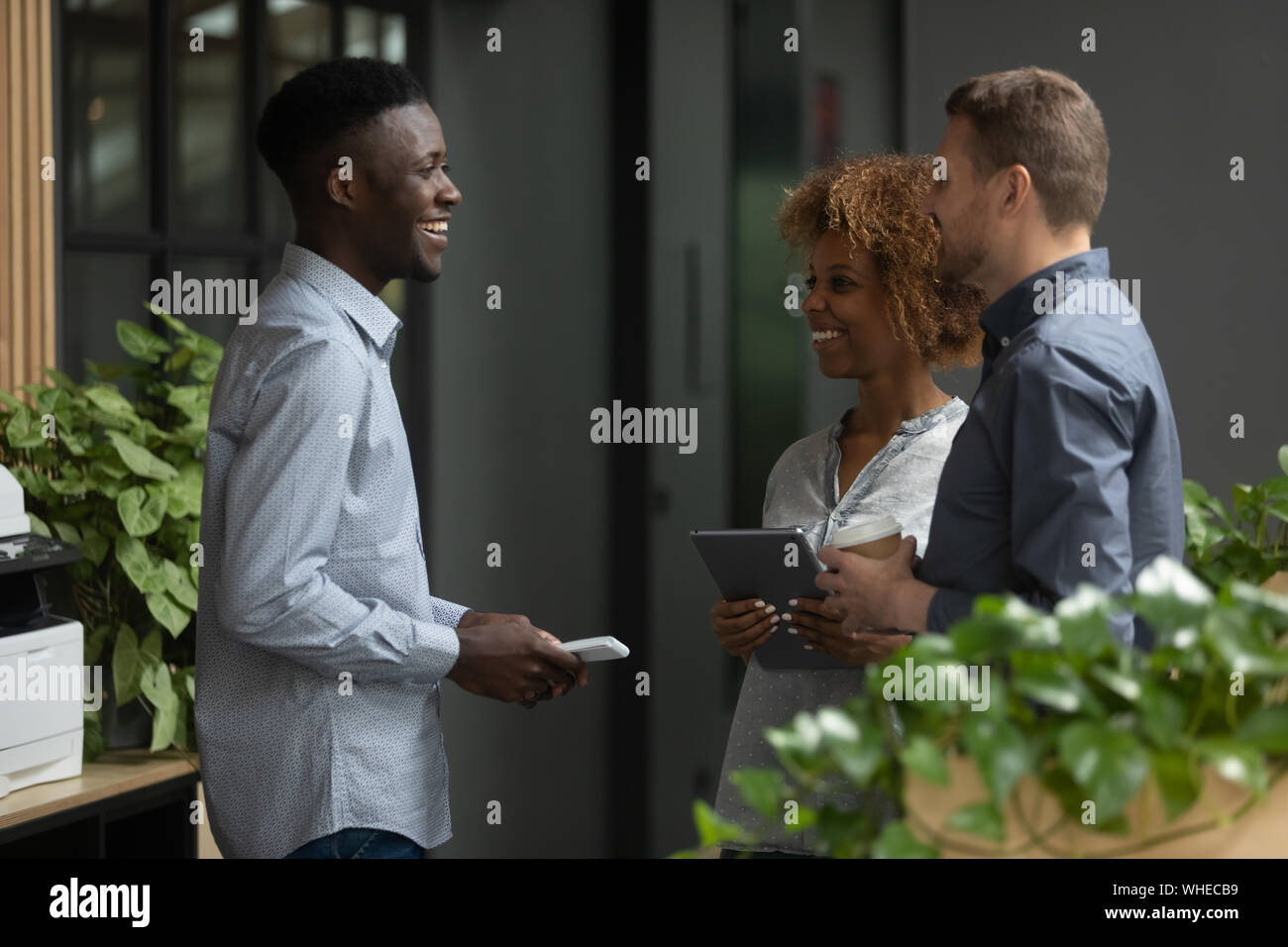 Three diverse happy colleagues talking laughing standing in office ...