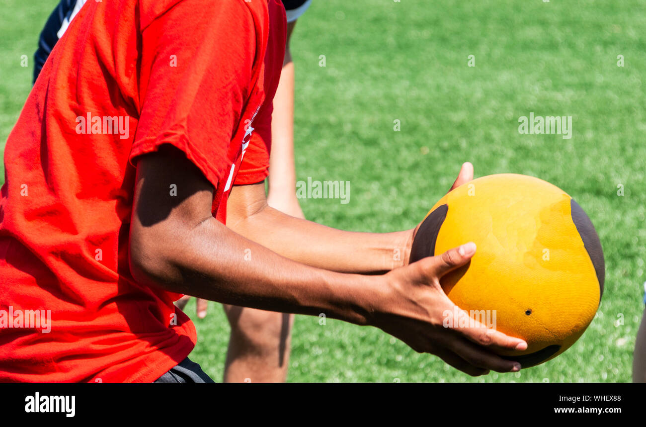 A teenage boy is playing catch with a medicine ball on a green turf ...