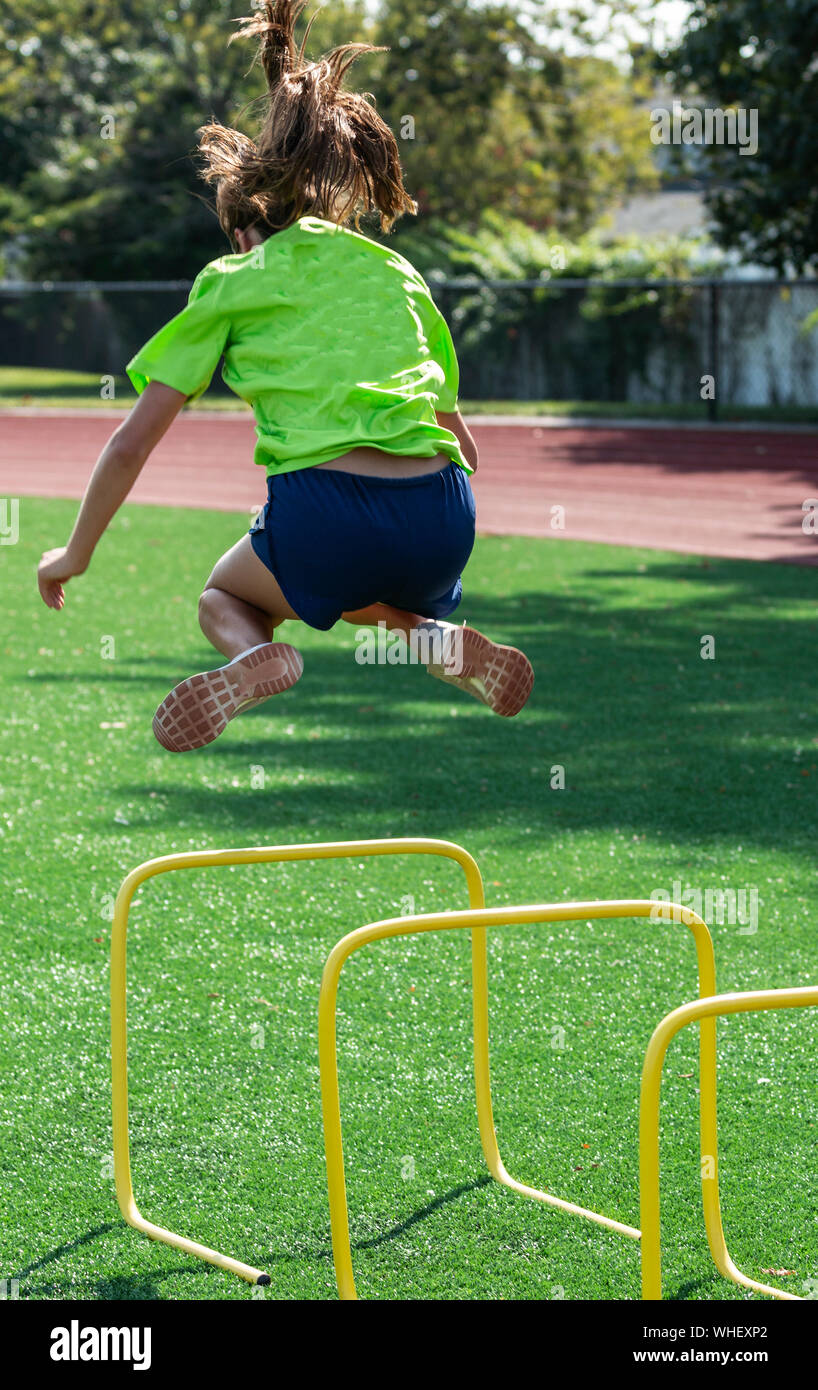 High school teenage girl is jumping over a two foot yellow mini hurdle ...