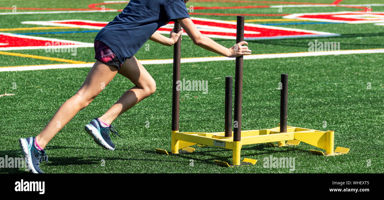 High school cros country runner is pushing a heavy sled across an turf ...