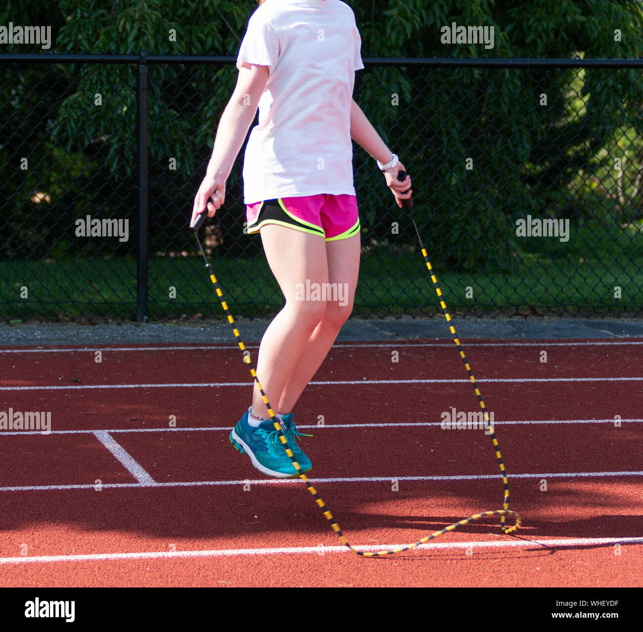 A teenage girl is using a black and yellow jump rope in the shade on a ...