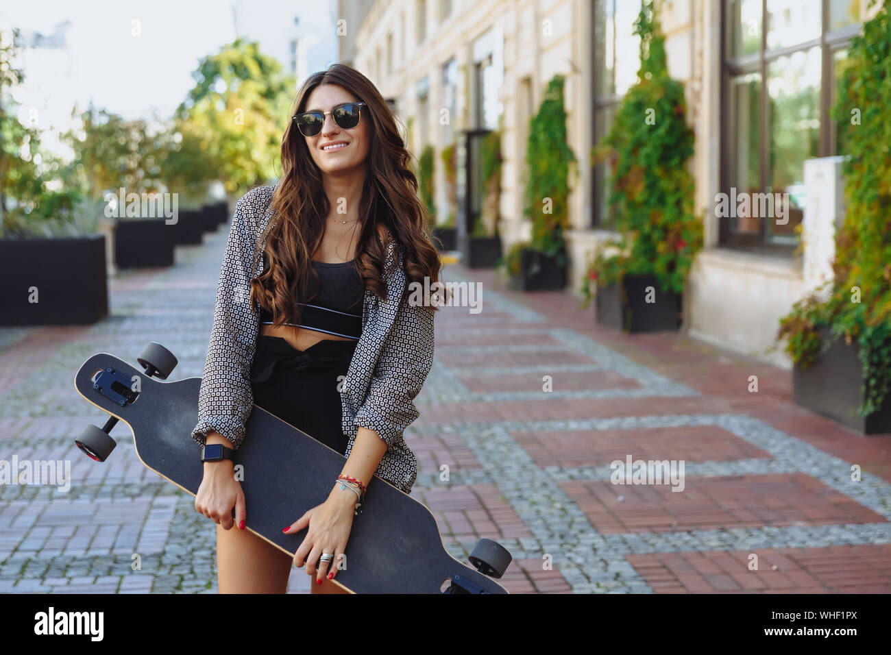 Beautiful young woman with longboard on the city street in sunny ...