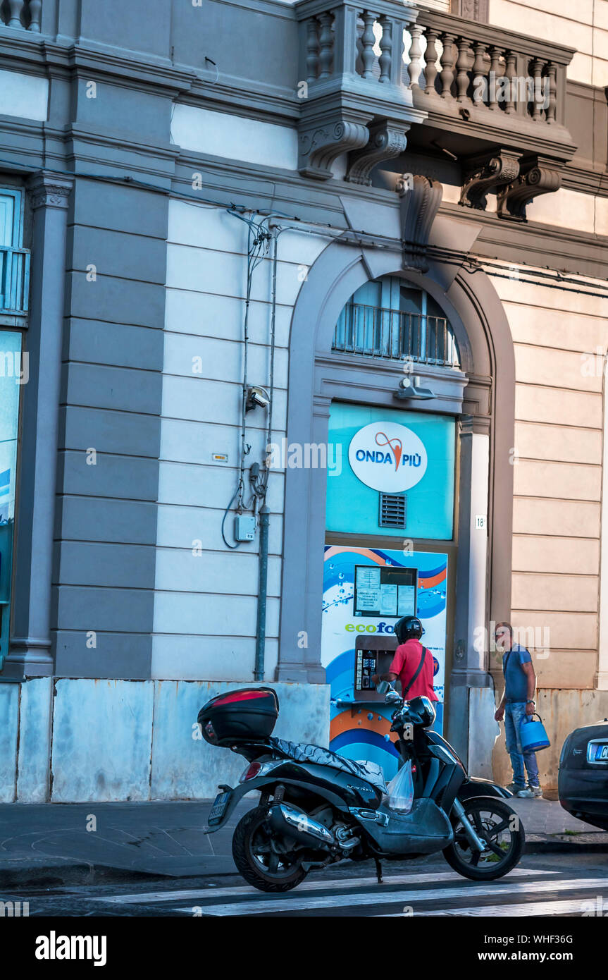 A motorcycle stands on the street as two men are at an ATM, Siracusa ...