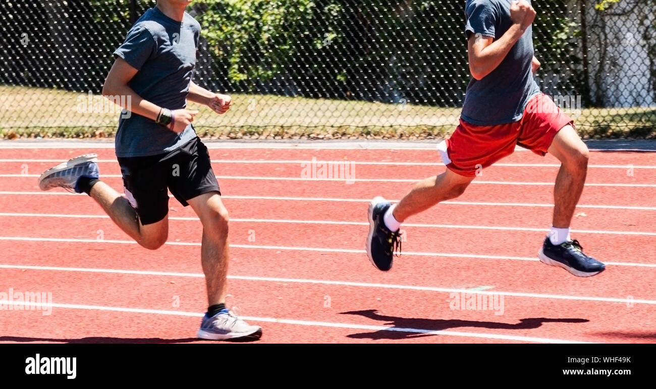 Two boys racing each other running clockwise on a red track on s sunny ...