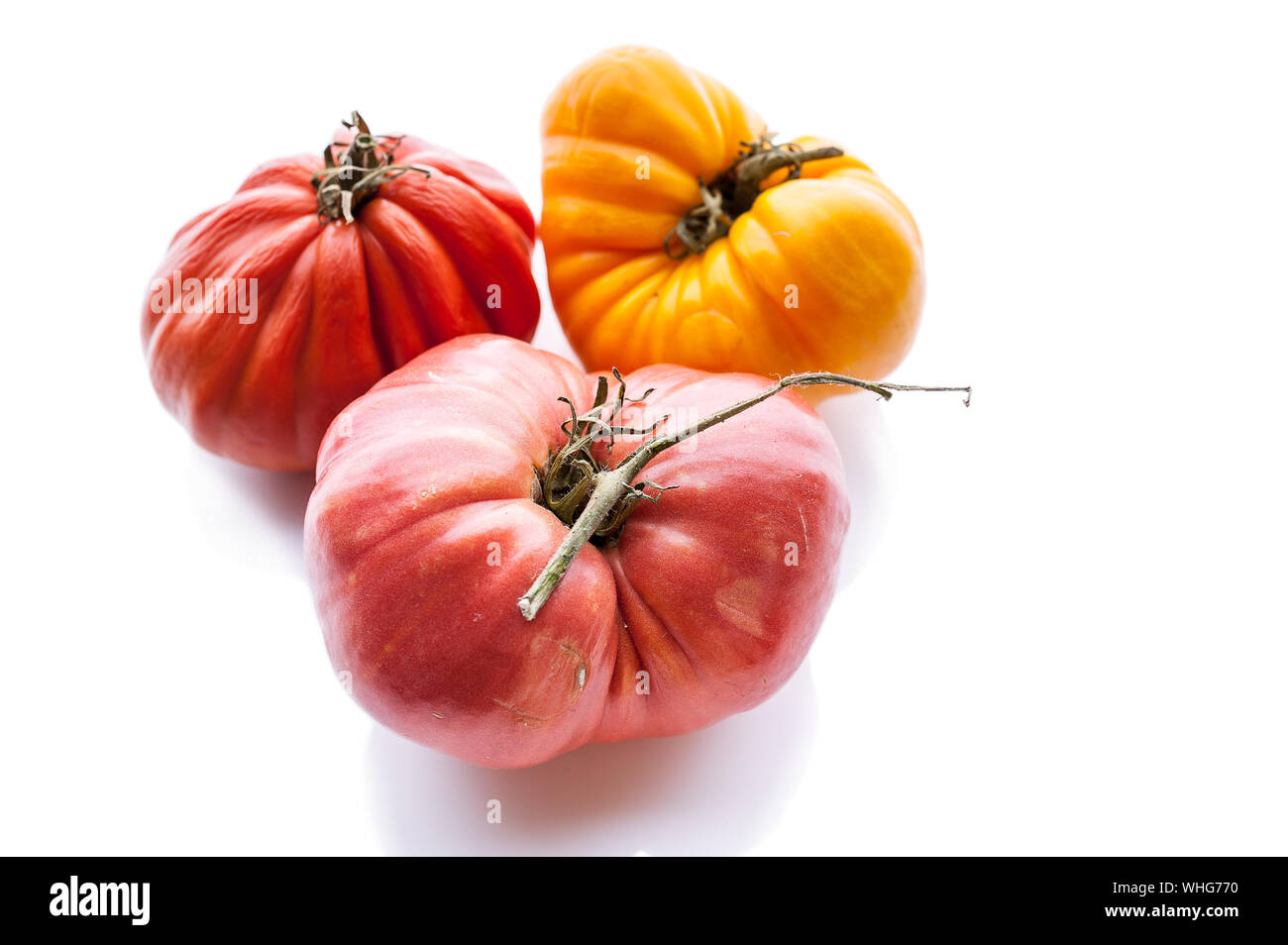 Three tomatoes of different colors and shapes on a white background ...