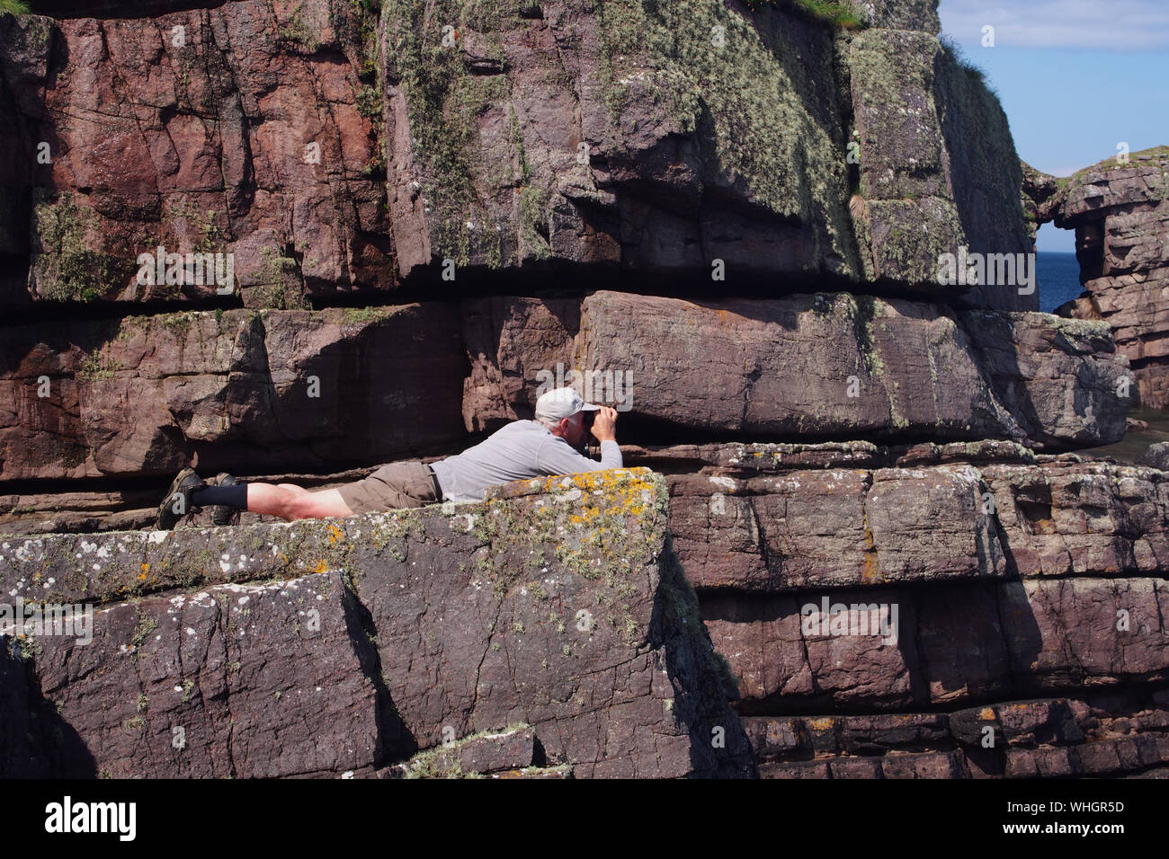 An older man laying face down on rocks looking out to deep blue sea ...