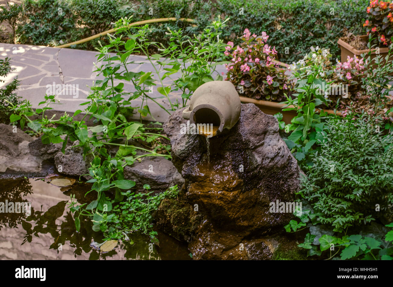 An artificial stream with running water from a clay pitcher lies on ...