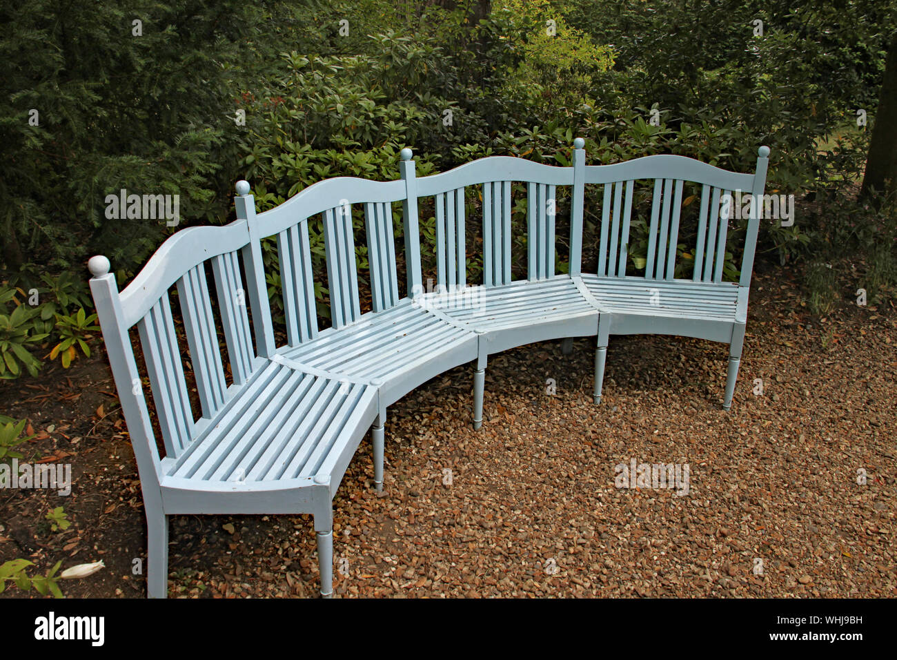 A blue curved bench in a shady area of a garden Stock Photo - Alamy