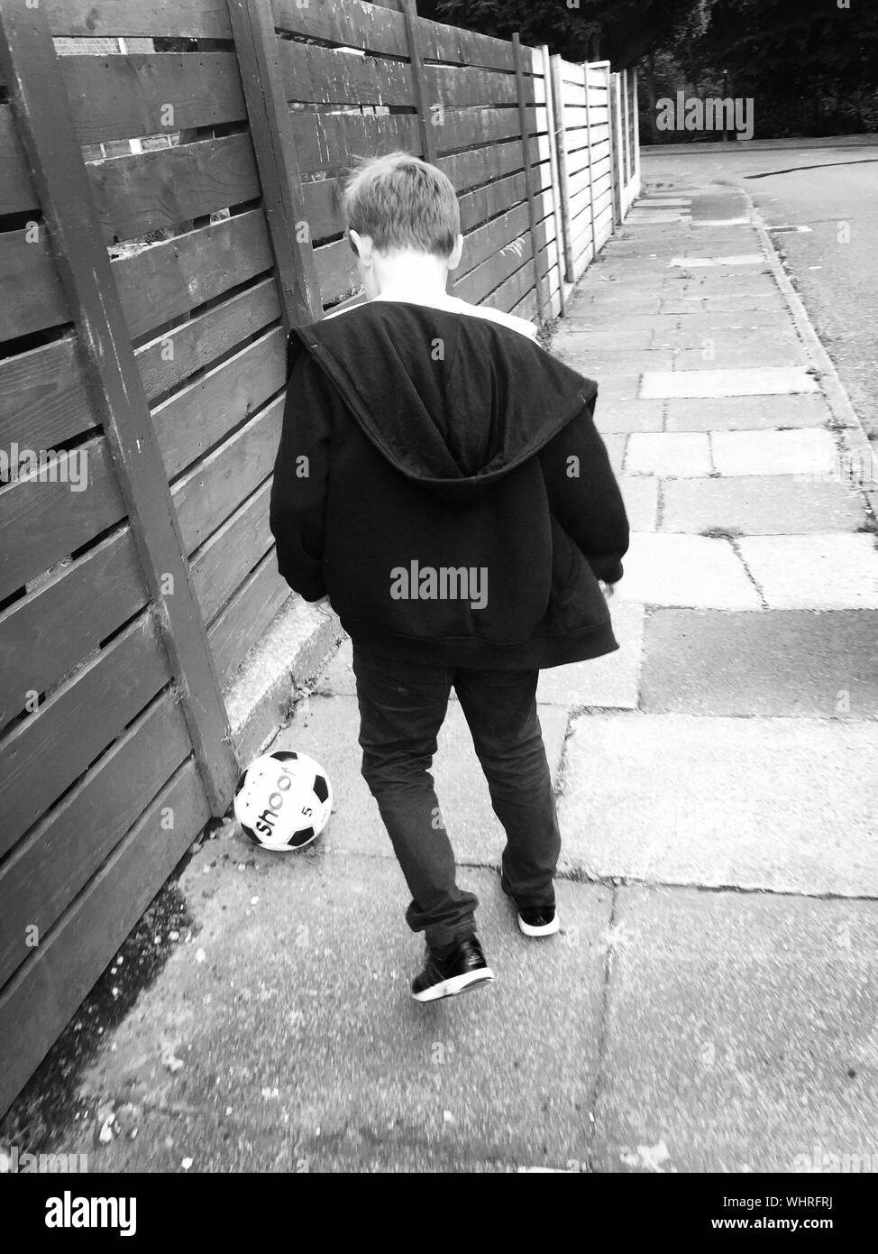 Rear View Of Boy Playing Soccer On Sidewalk Stock Photo - Alamy