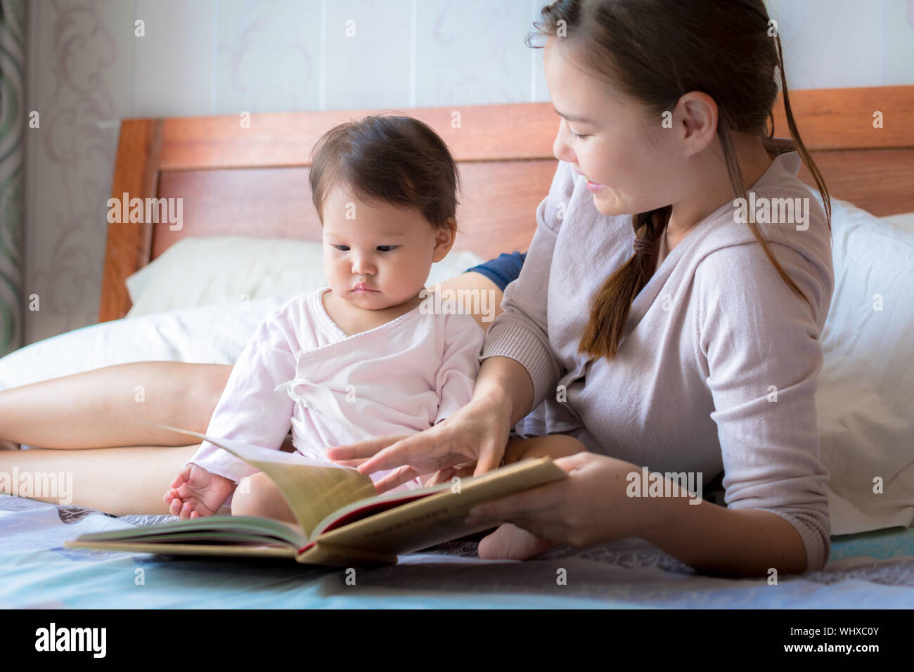 a mom reading a story to her baby on a soft bed. child concentrating on ...