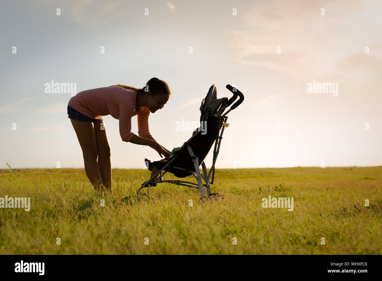 mother walking her baby in stroller, outside at a beautiful park during ...