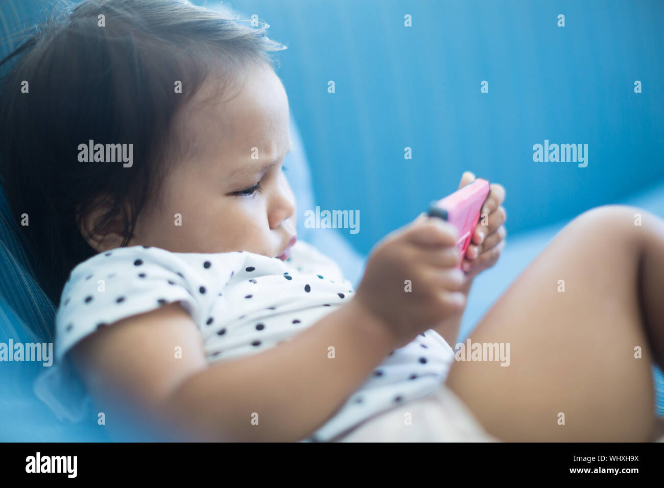 Young girl is slouched on a couch while watching tv on a cellphone ...