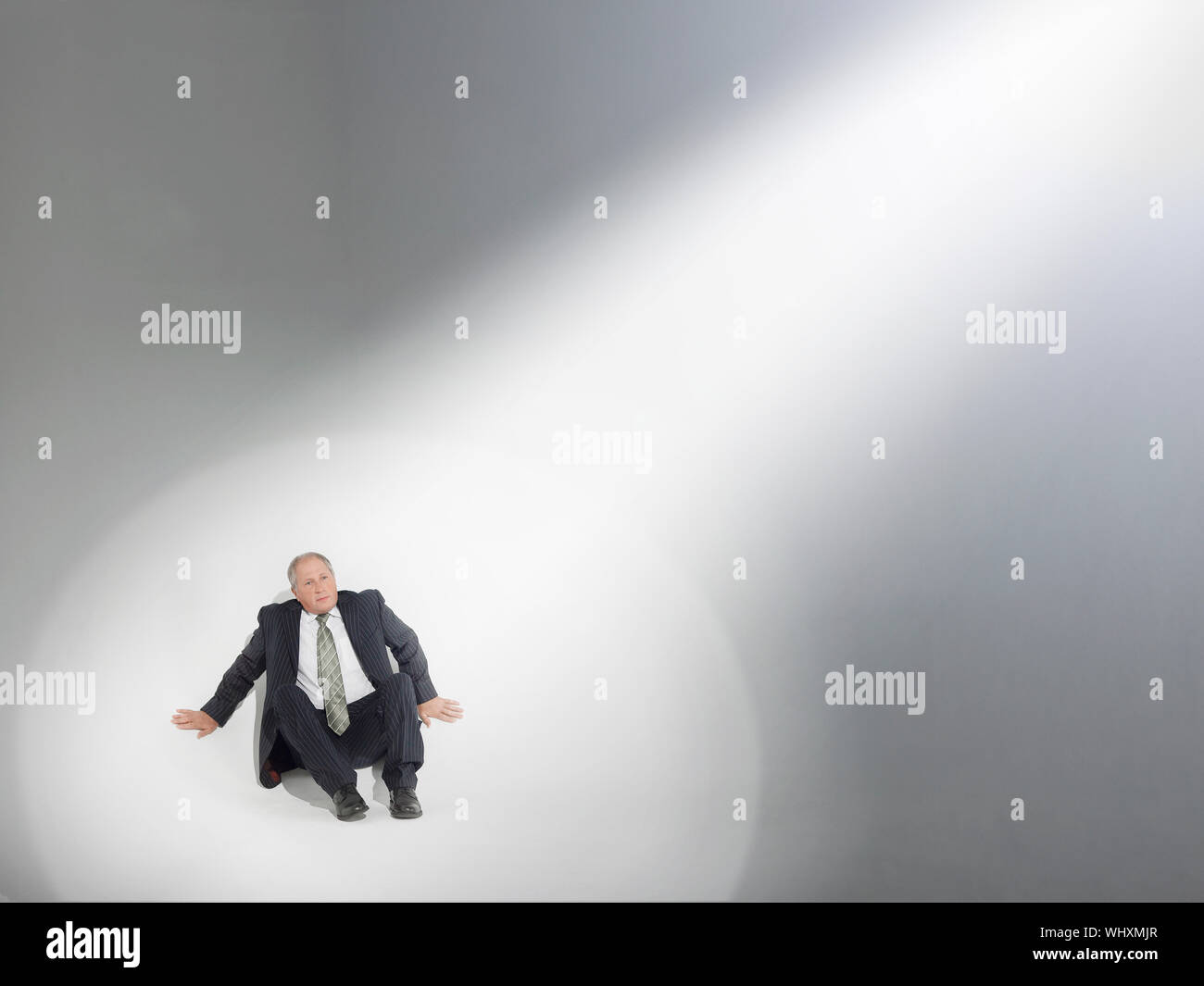 Businessman sitting and looking up at source of spotlight Stock Photo ...