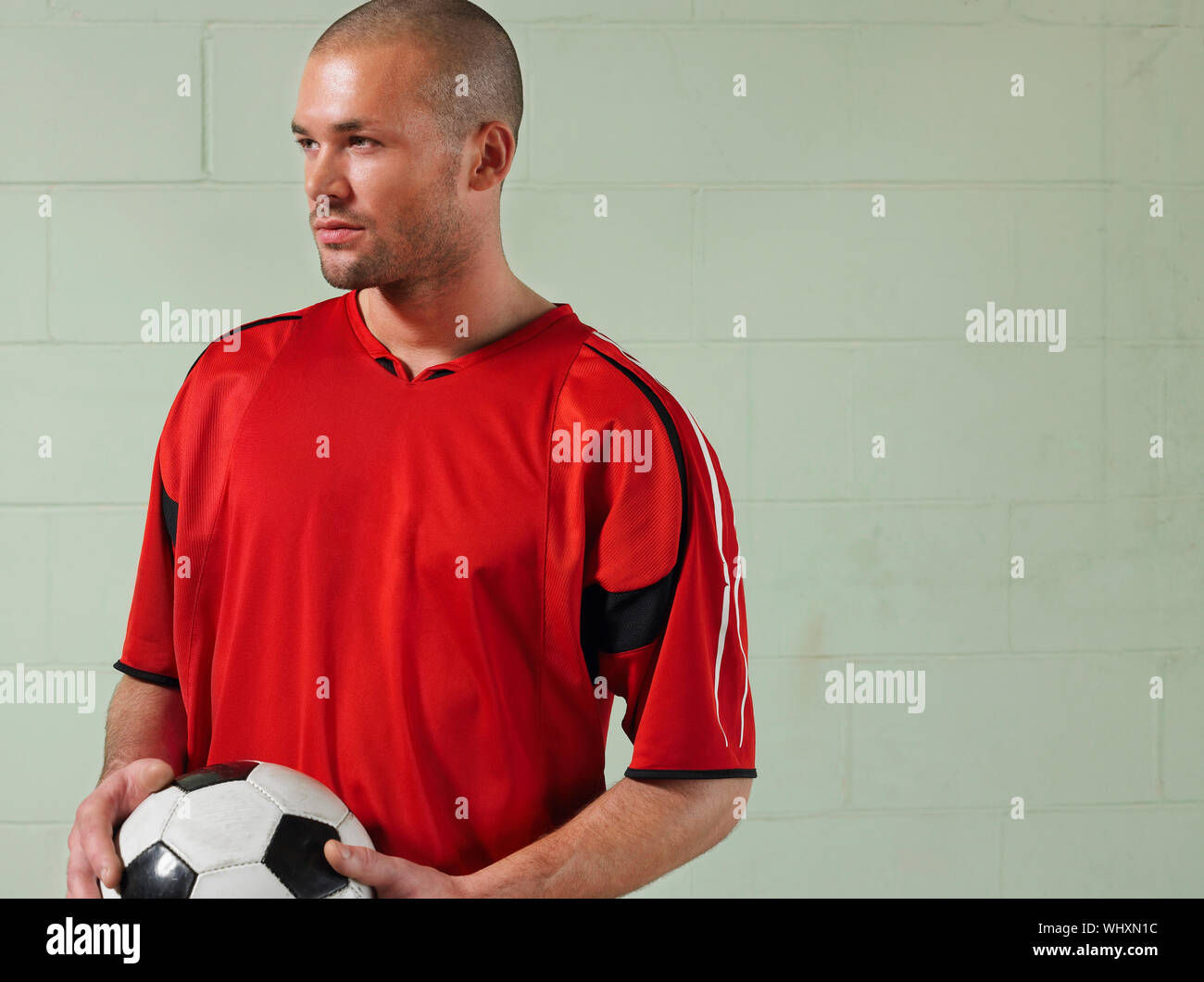 Serious soccer player holding ball against green wall Stock Photo - Alamy