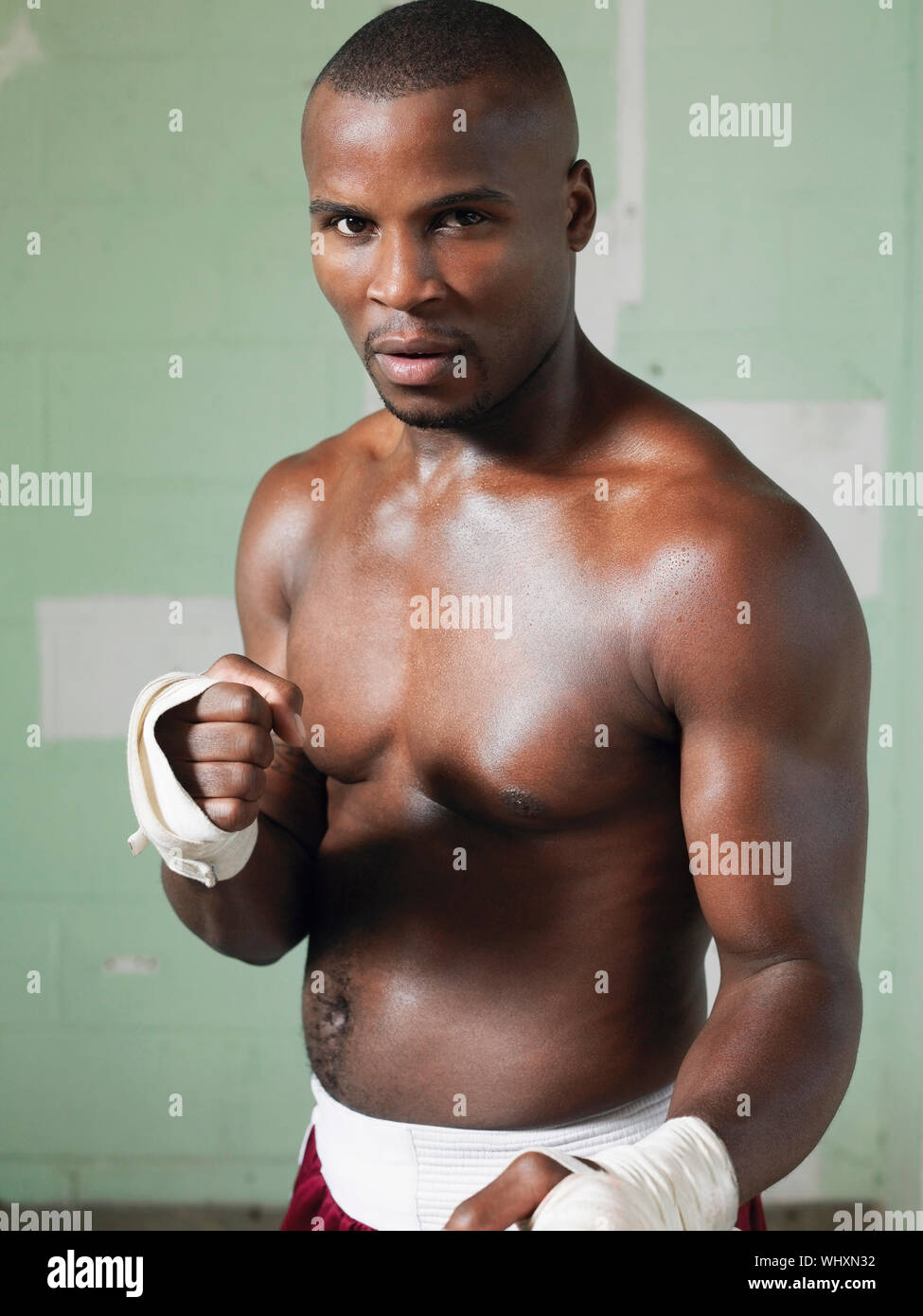 Portrait of a bare chested African American boxer against green wall ...