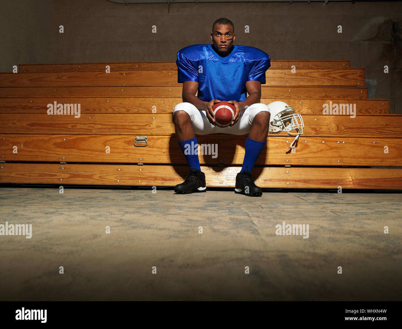 Portrait of an American football player sitting on bench with ball ...