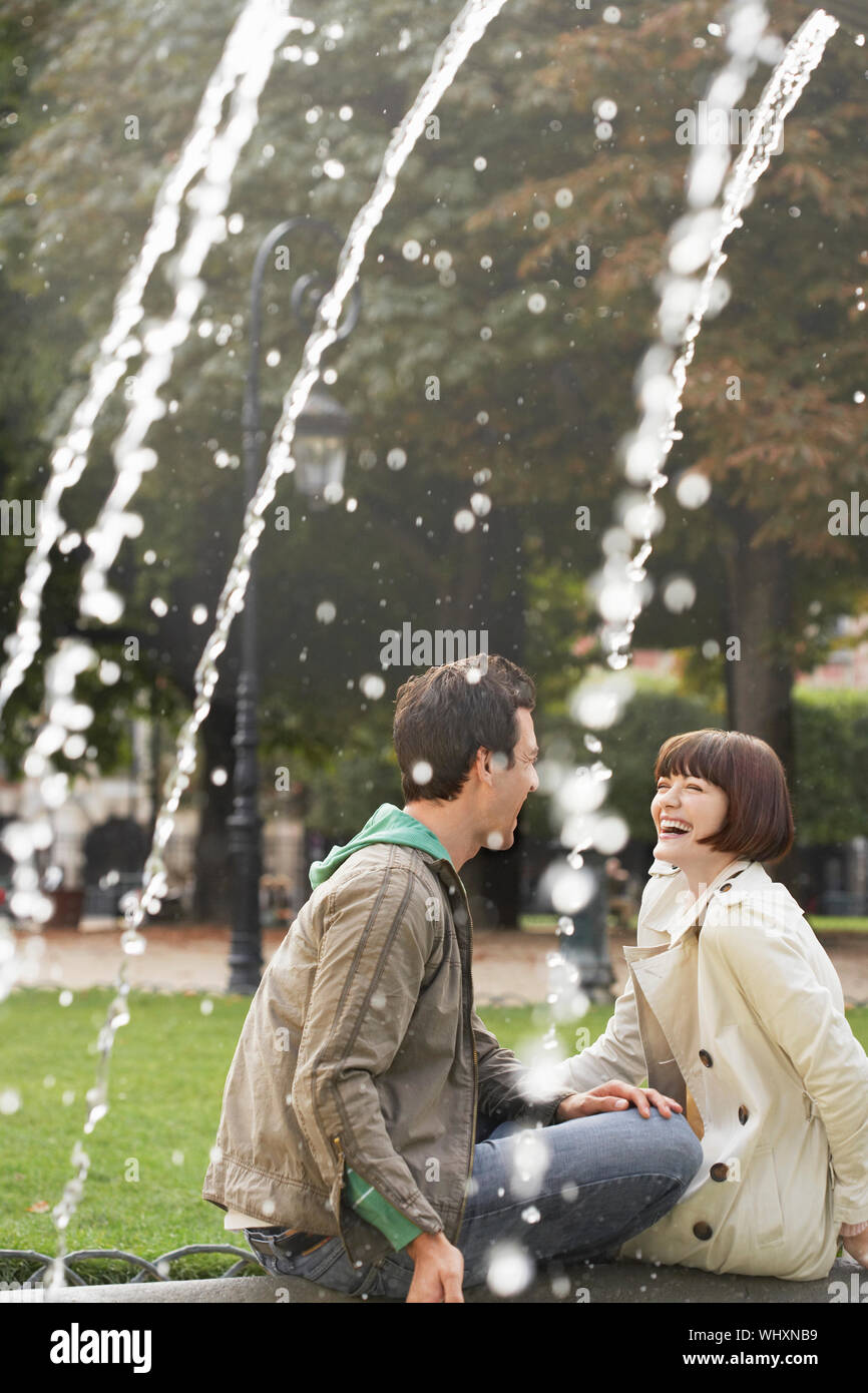 Side view of a cheerful couple laughing on fountain edge Stock Photo ...