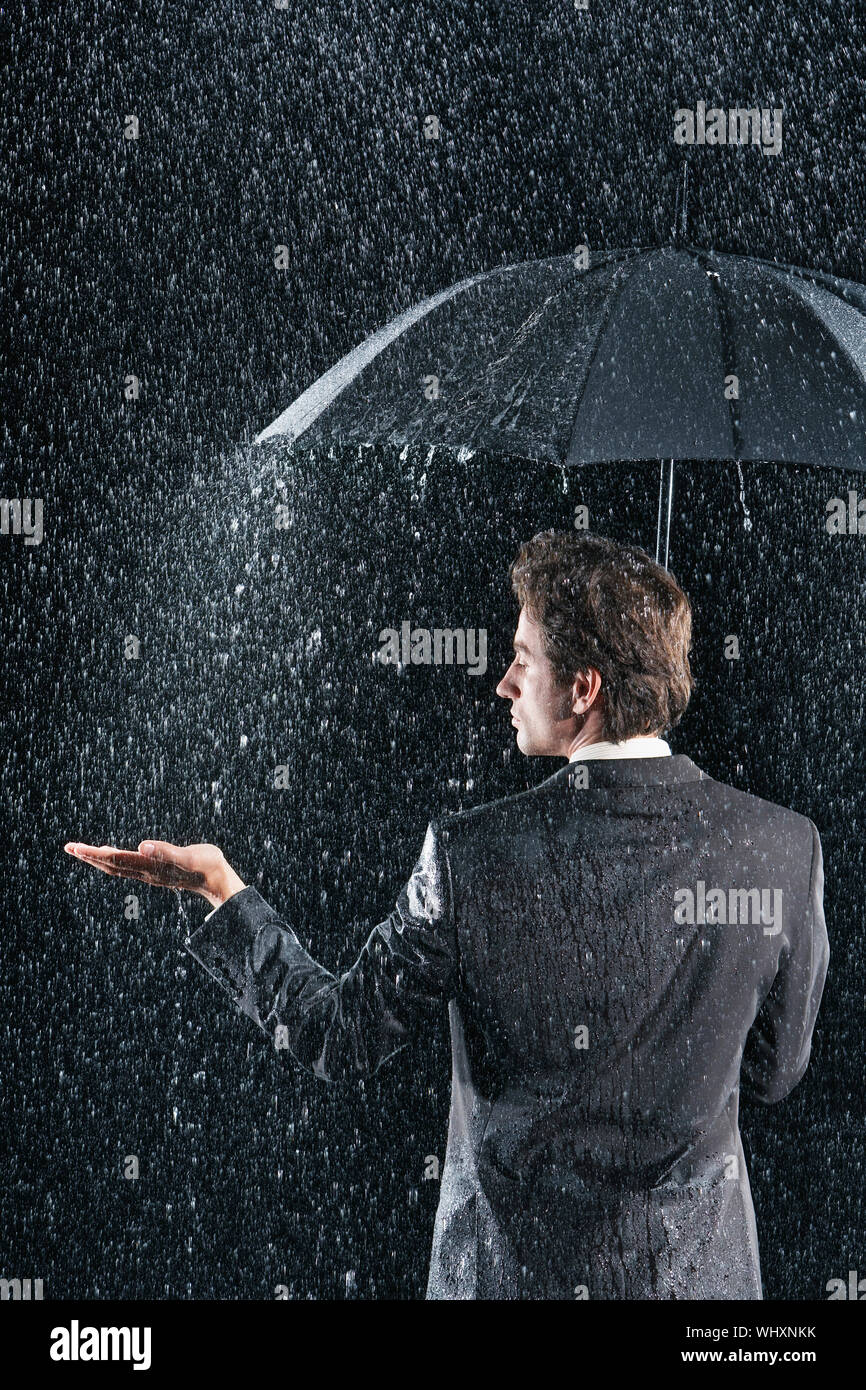 Rear view of a businessman sticking hand out from under umbrella to ...