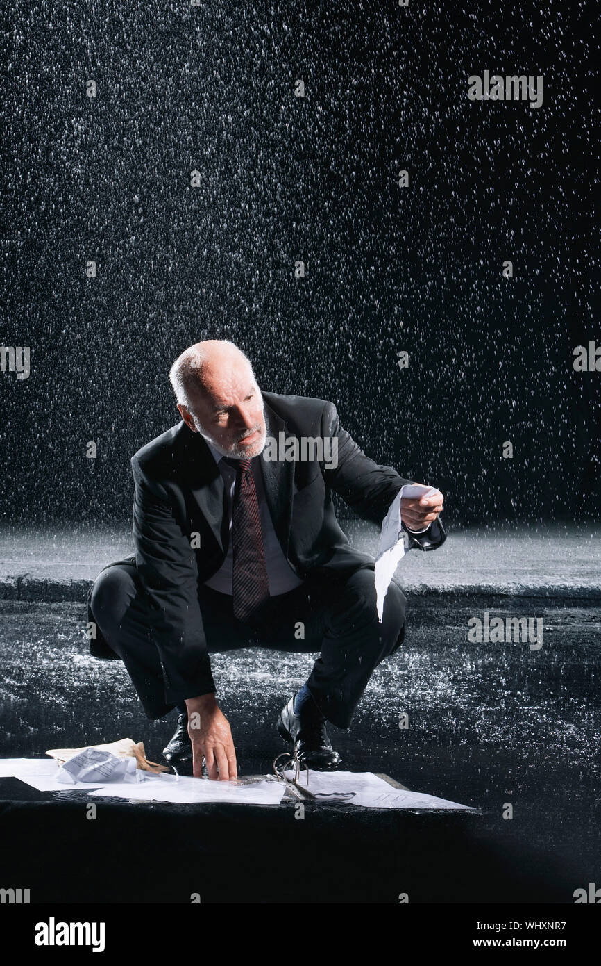 Middle aged businessman picking up soaked documents during downpour ...