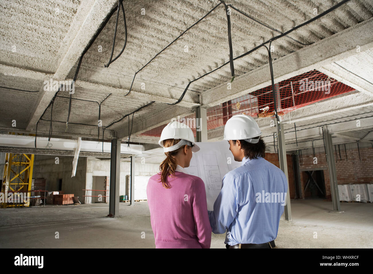 Rear view of architect and construction manager reading blueprint at ...