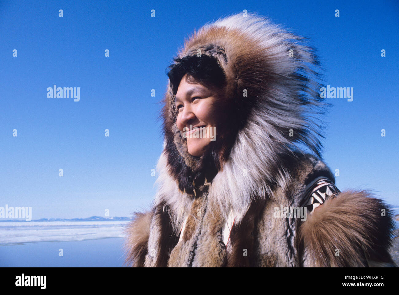 Smiling Eskimo woman wearing traditional clothing in wind against clear ...