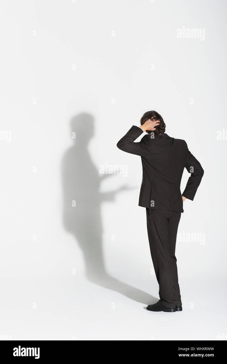 Full length rear view of a young businessman arguing with own shadow ...