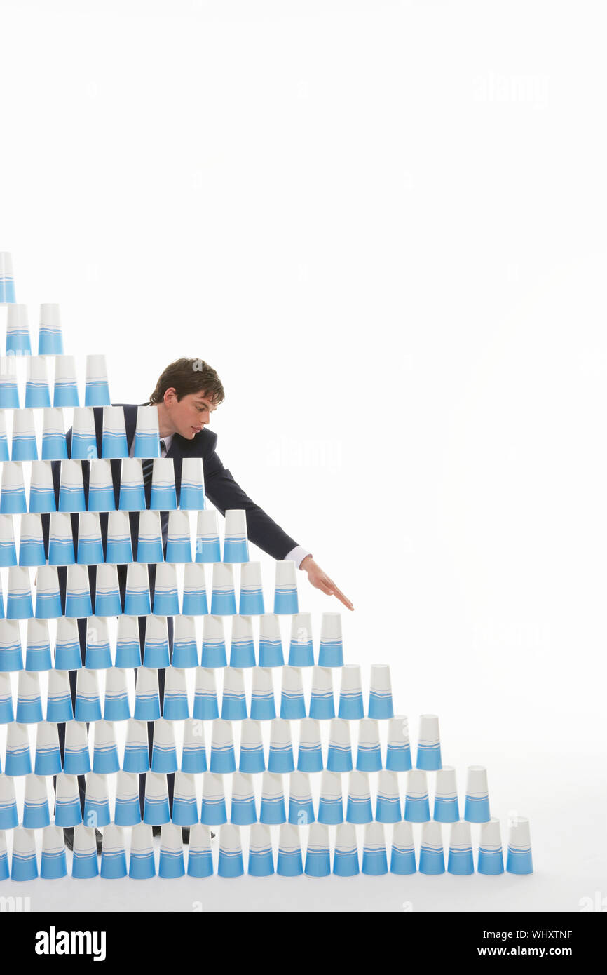 Young businessman stacking plastic cups into a pyramid against white ...