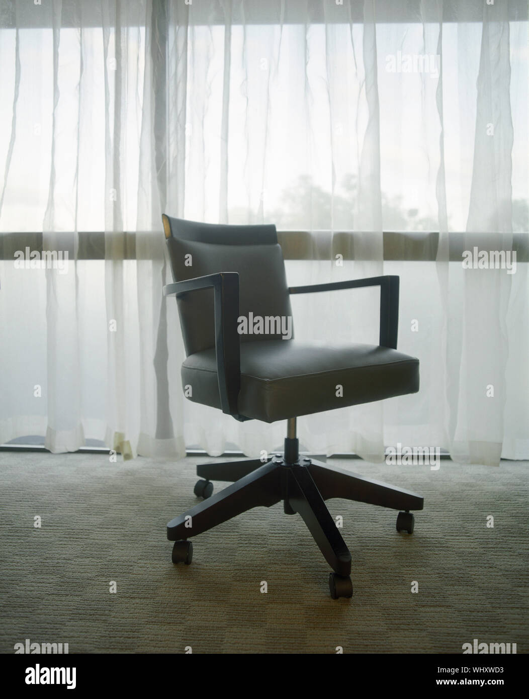 Empty office chair in front of curtained window Stock Photo - Alamy