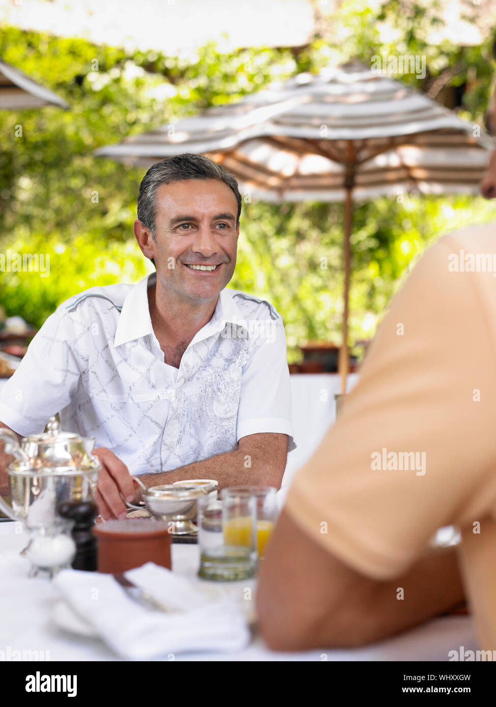 Two men sitting at outdoor dining table and talking Stock Photo - Alamy