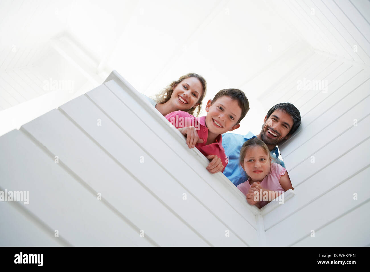 Low angle view of happy parents with children looking over white wall ...