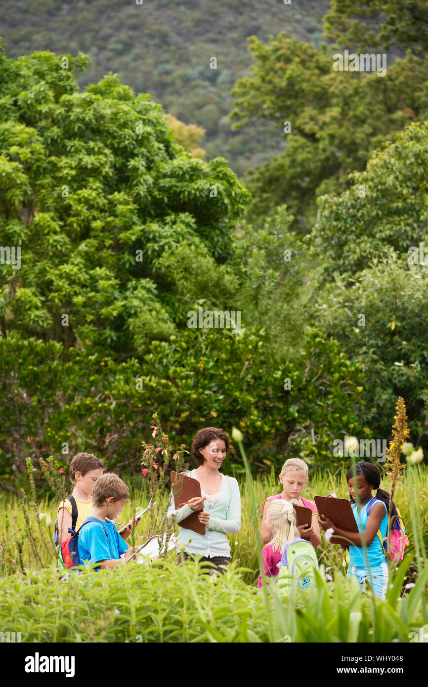 Young teacher with children preparing notes on clipboards during field ...
