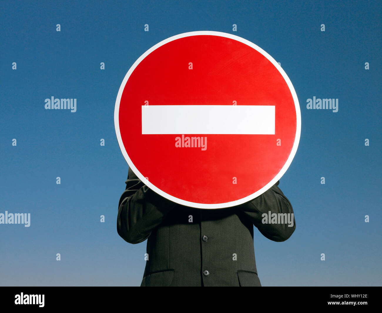 Businessman holding 'No Entry' sign in front of face against clear sky ...
