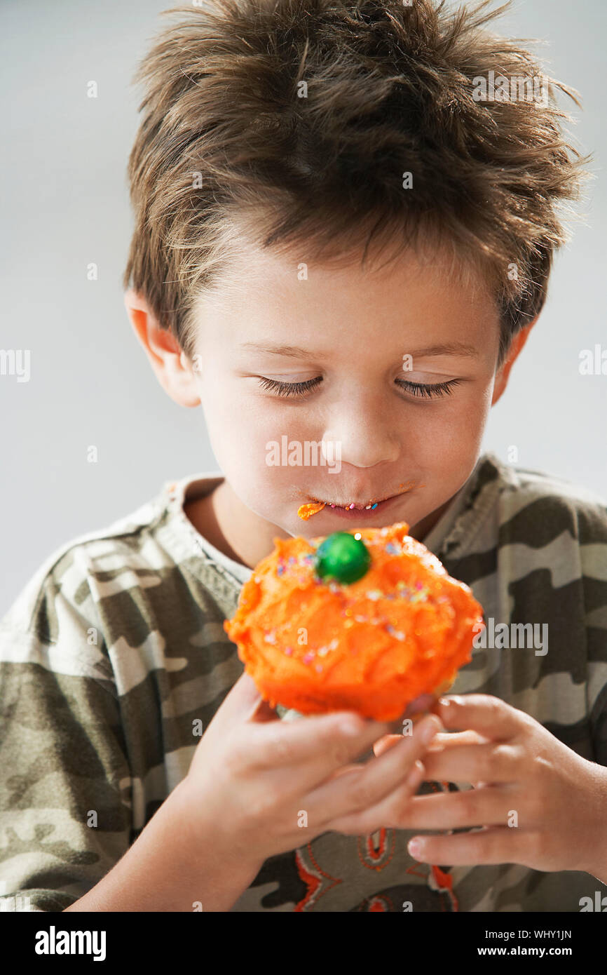 Young boy eating cupcake isolated on gray background Stock Photo - Alamy