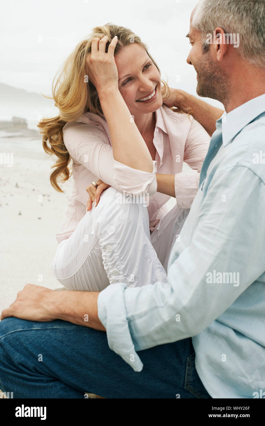 Happy Romantic Couple Looking At Each Other While Sitting On Beach