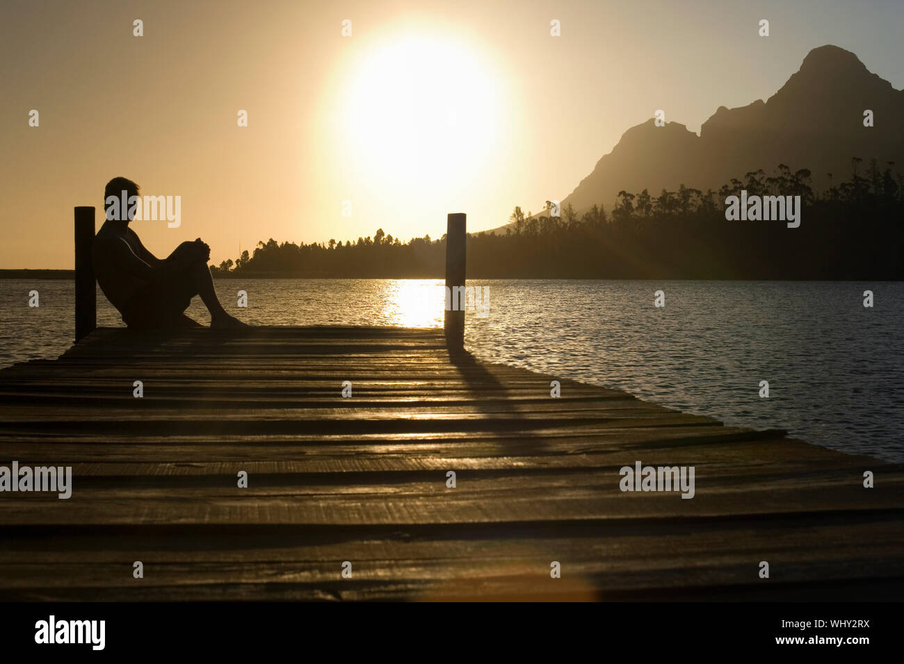 Side view of man sitting on dock by lake enjoying sunset Stock Photo ...
