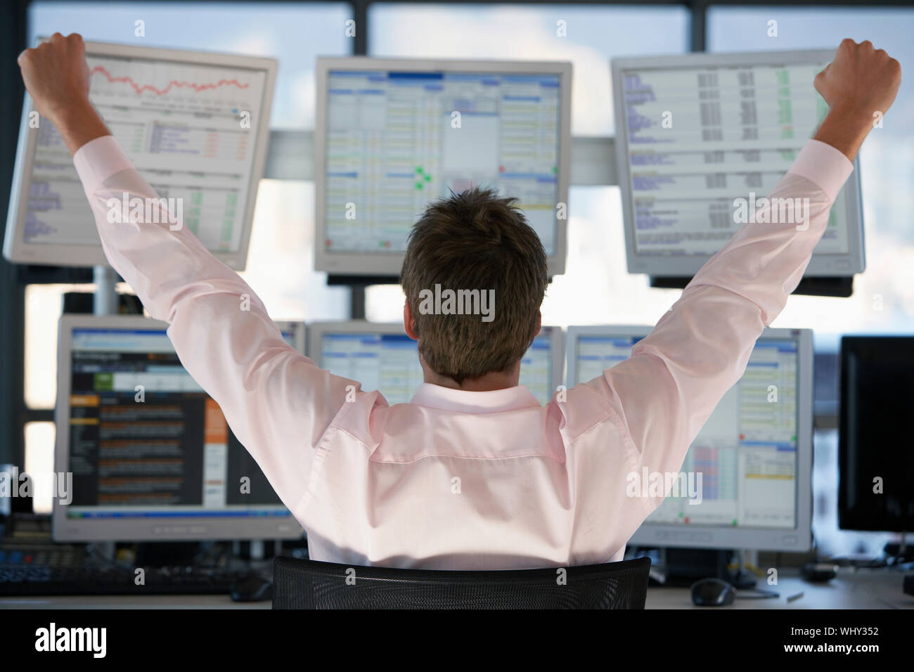 Rear view of stock trader with hands raised looking at multiple computer screens Stock Photo - Alamy