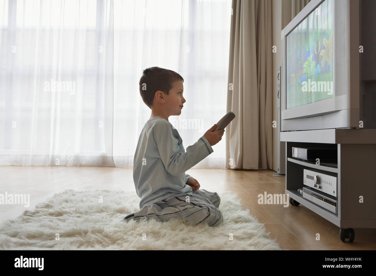 Side view of a boy sitting on floor and watching cartoons in television ...