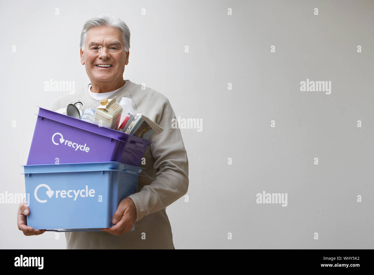 Portrait of a mature man carrying recycling bin against gray background ...
