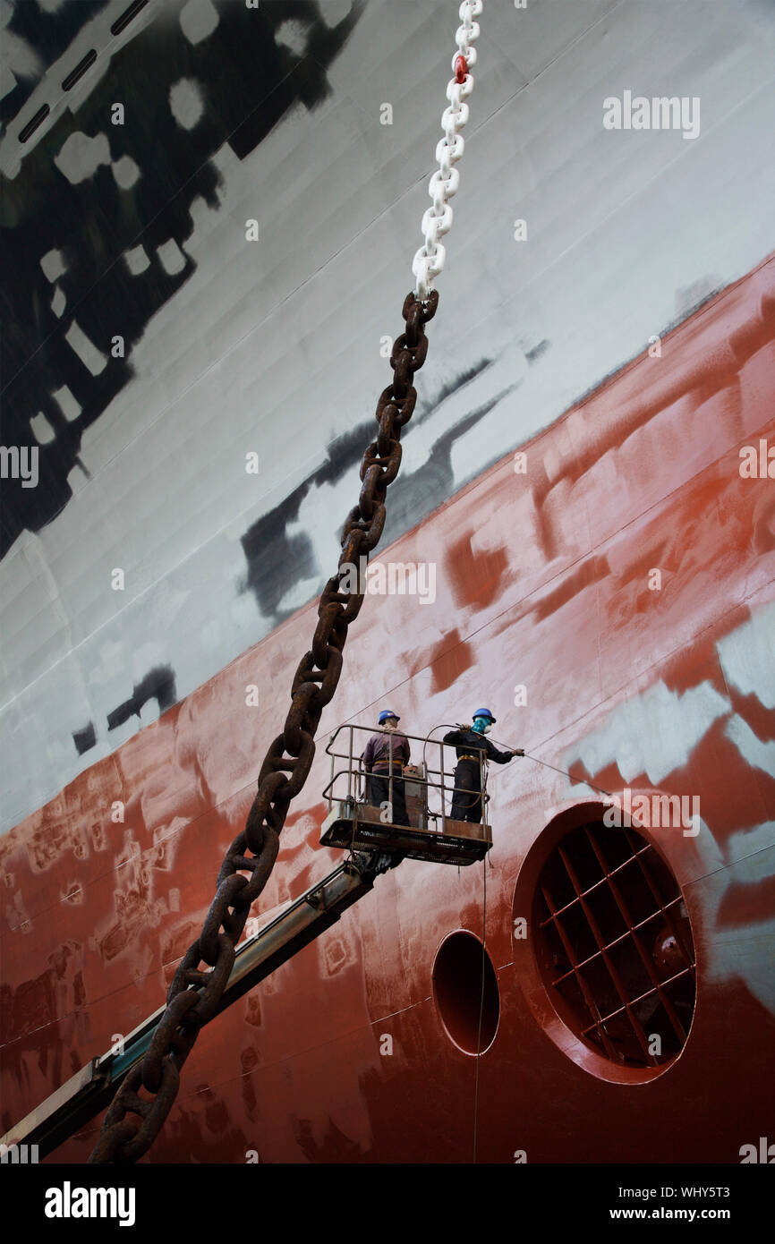 Two men in cherry picker working at ship in dry dock low angle view ...