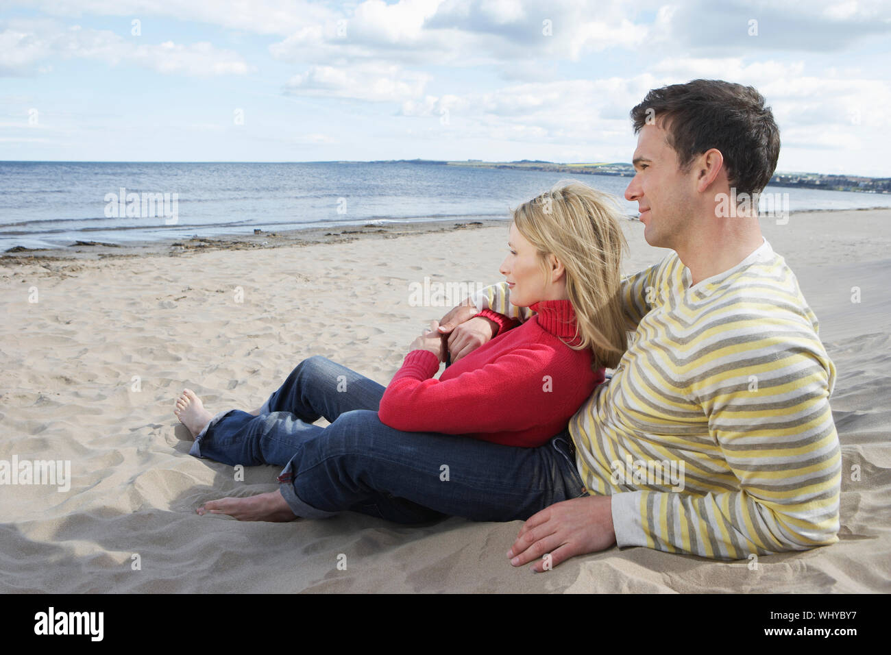 Side view of happy loving couple relaxing on sandy beach looking at ...