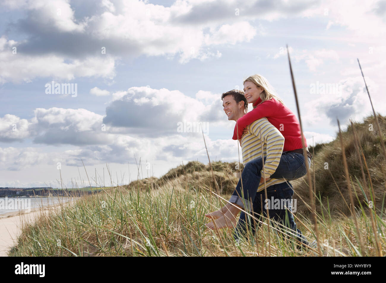 Side view of happy couple enjoying piggyback ride on beach Stock Photo ...