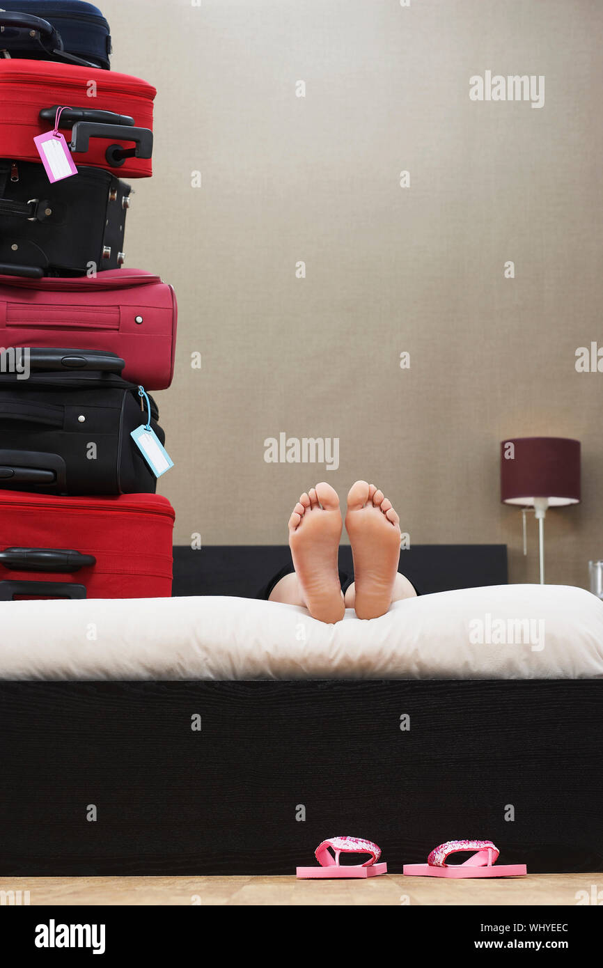 Low section of woman lying down in bed next to stack of suitcases Stock ...