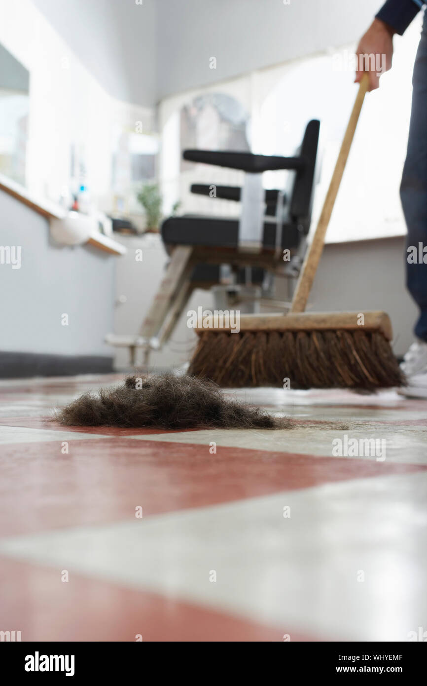 Hairdresser sweeping hair clippings on floor in barber shop Stock Photo ...